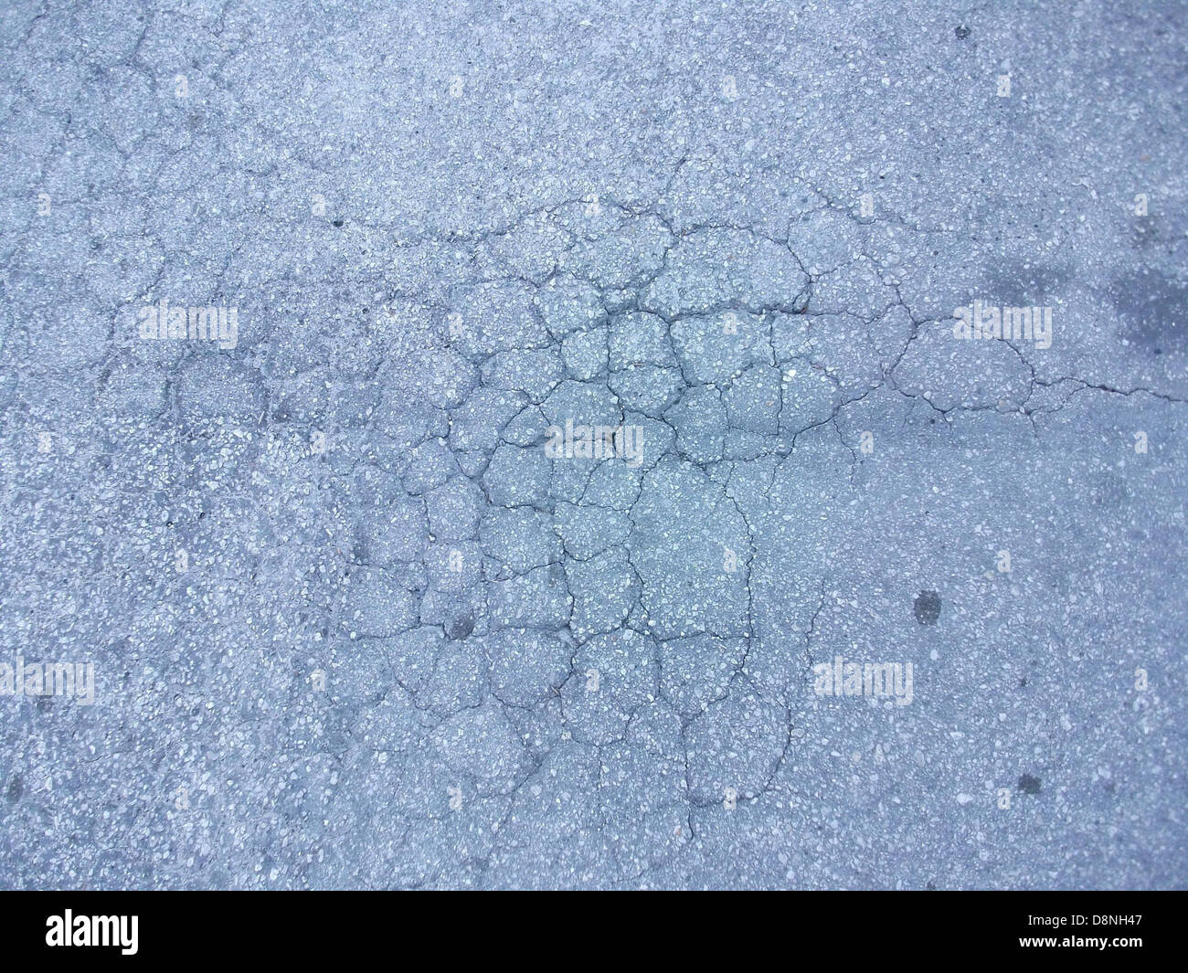 A close-up of worn, cracked asphalt pavement, showing signs of age and ...