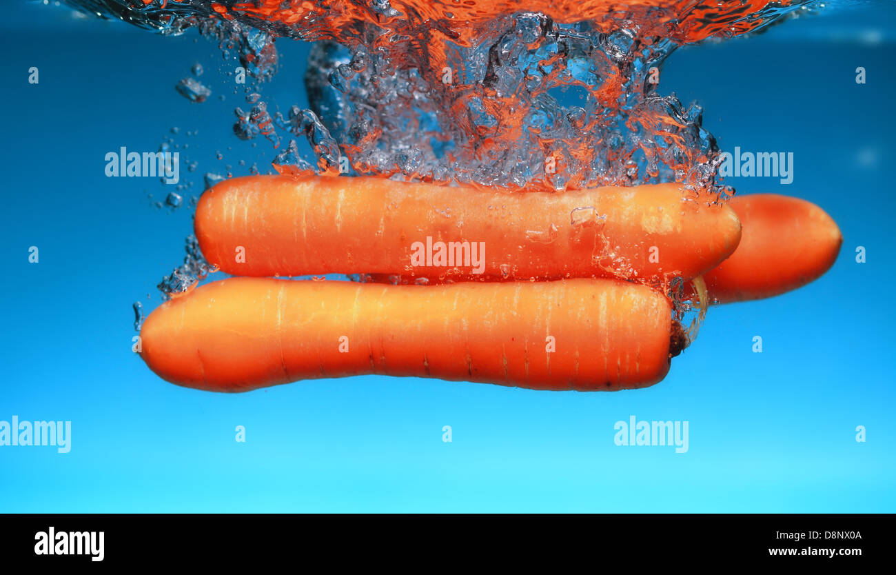Carrot in the water splash over blue background. Healthy food and ...