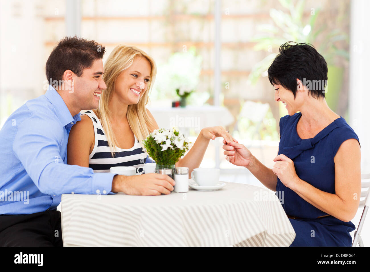 happy young woman with fiancé showing her engagement ring to her mother ...