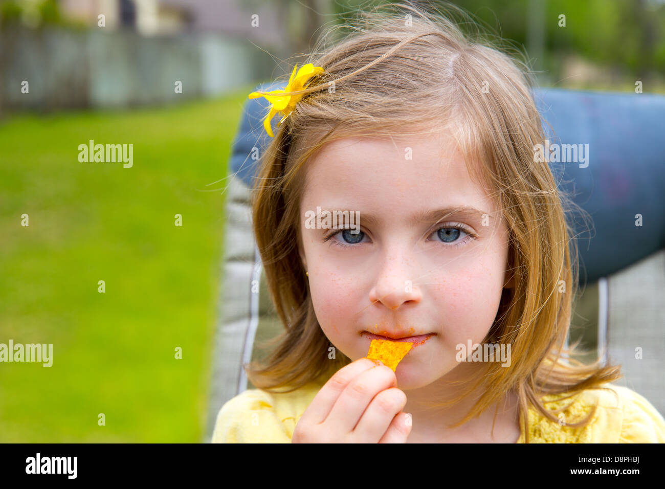 Blond kid girl eating corn snacks in outdoor park in lawn background ...