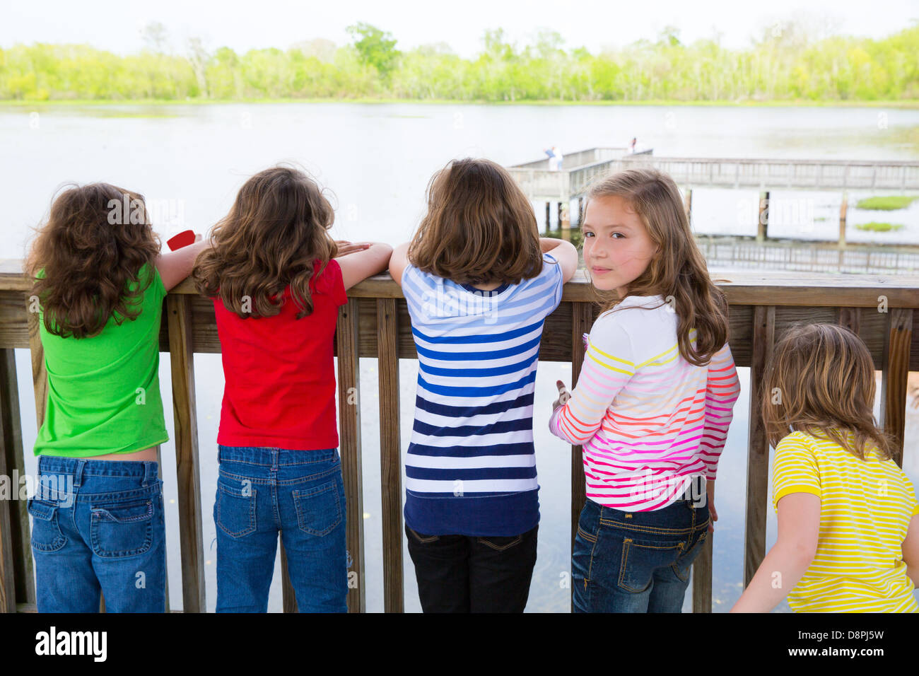 Children girls rear view looking at lake on railing and one looking ...