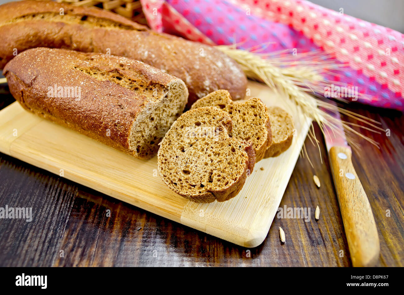 Rye baguettes on a board with a knife, wicker basket, stalks of rye, a ...