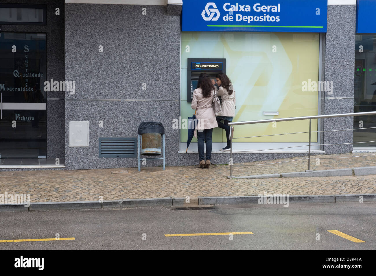 Two young woman at the Caixa Geral de Depositos cash dispensing machine ...