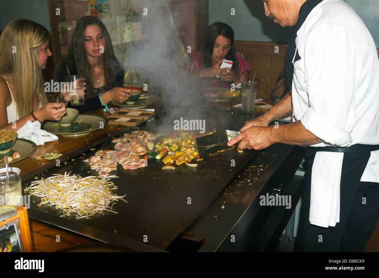 A chef preparing Japanese barbecue for bored young women Stock Photo ...