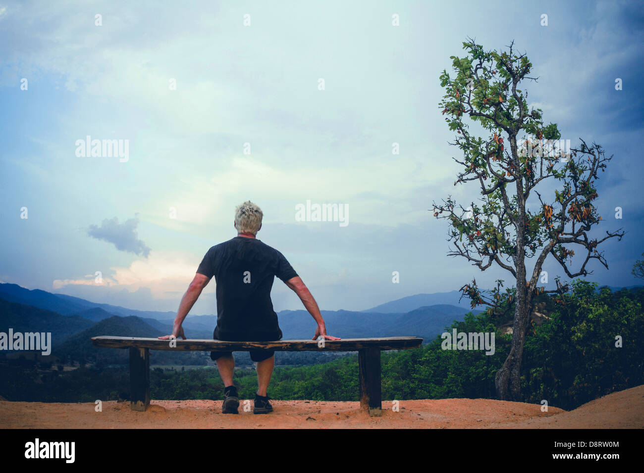 Man sitting alone on beach looking at view with back to viewer. No face ...