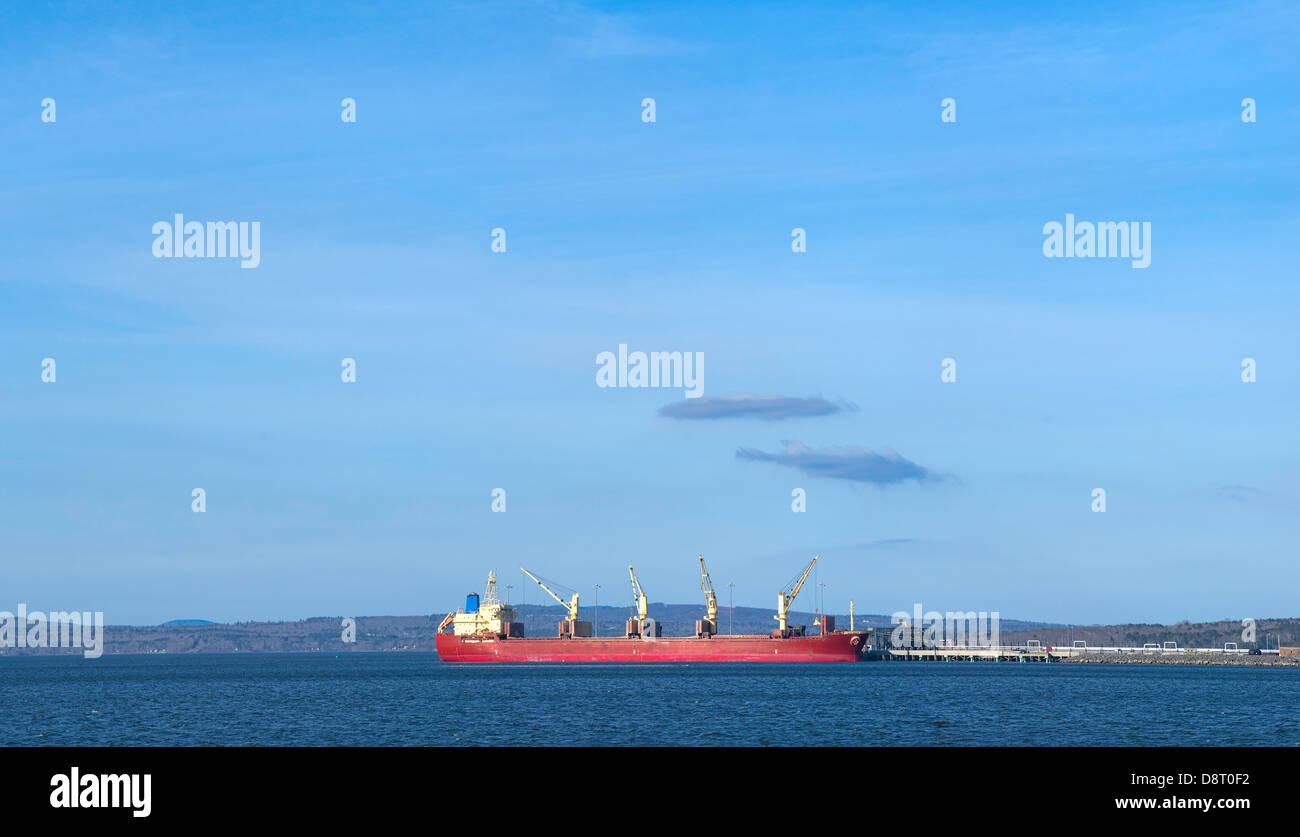 A large cargo ship with a red hull and white superstructure docked at a ...