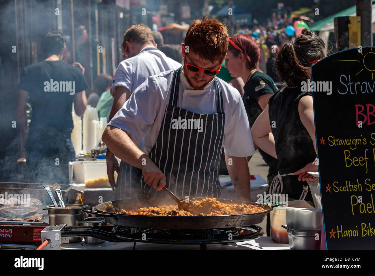 Chef cooking a pan of paella and and a grill of hamburgers on an ...