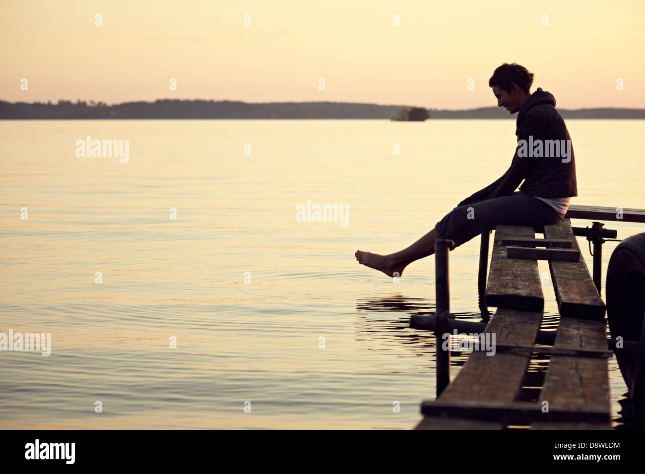 Young woman sitting on dock at sunset Stock Photo - Alamy