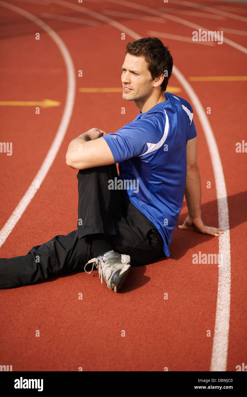 Male athlete sitting on running track Stock Photo - Alamy