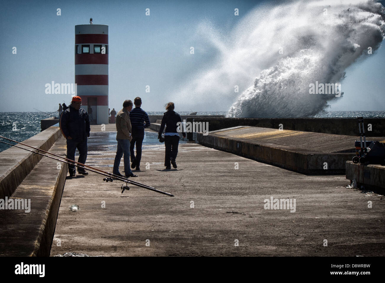 Huge wave hitting on harbor with lighthouse on the back and people ...