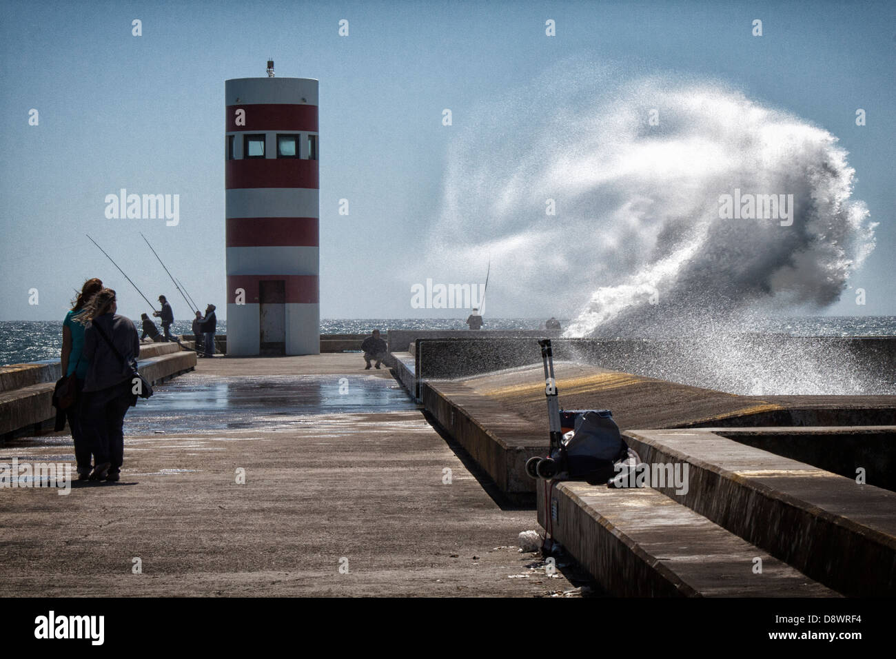 Huge wave hitting on harbor with lighthouse on the back and people ...