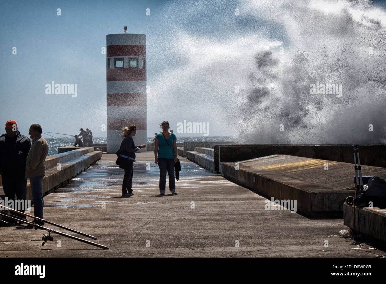 Huge wave hitting on harbor with lighthouse on the back and people ...