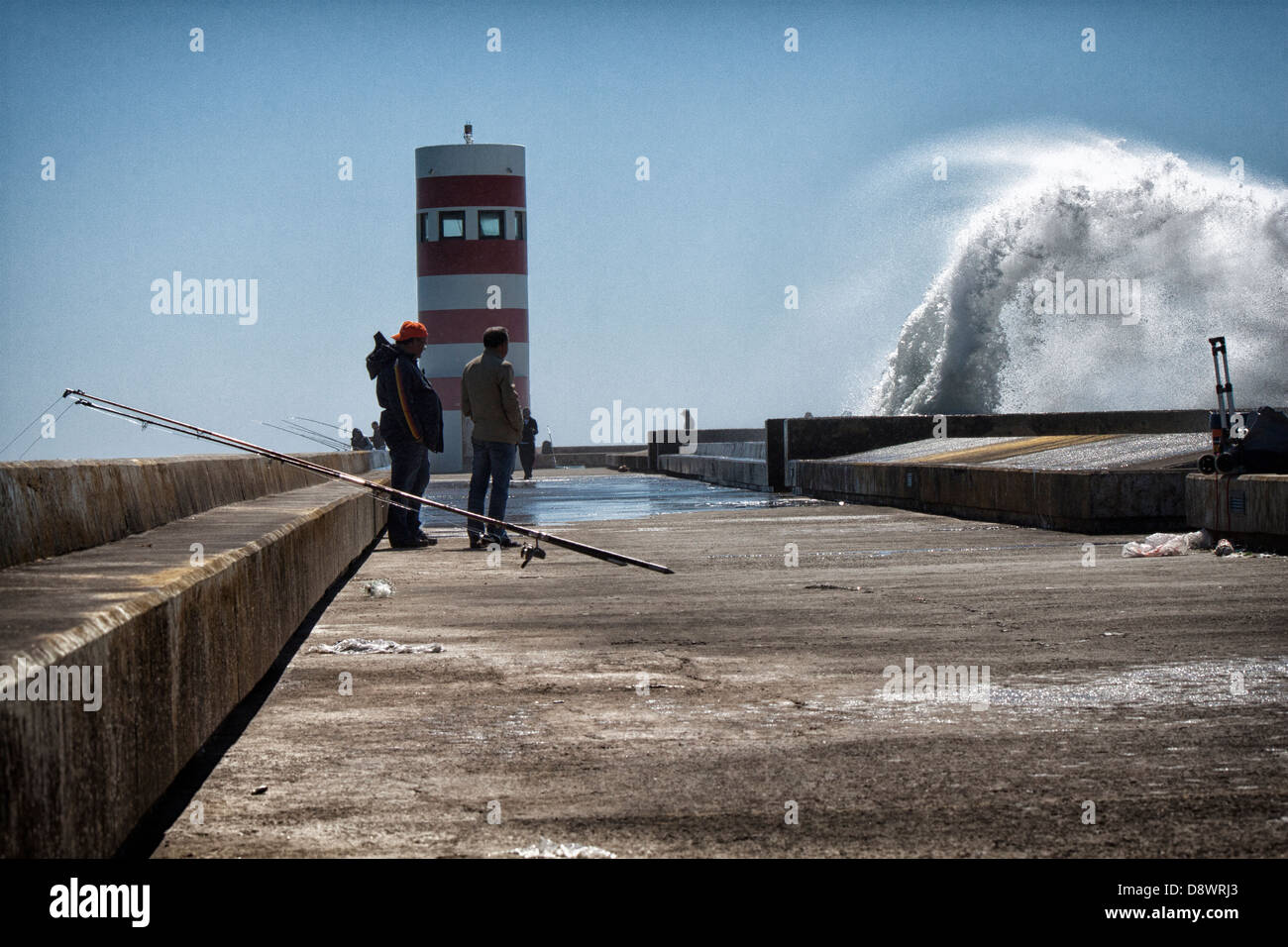 Huge wave hitting on harbor with lighthouse on the back and people ...