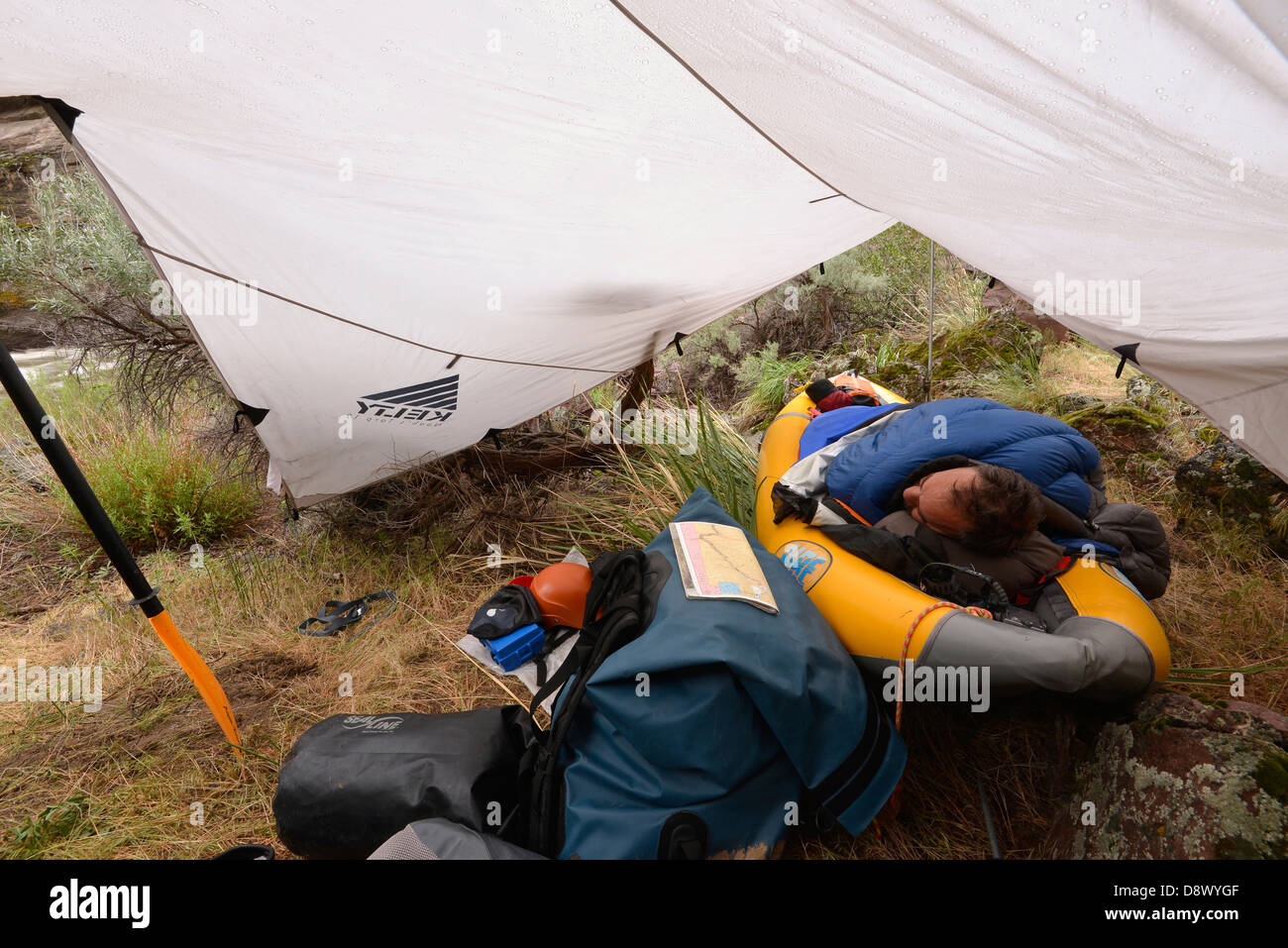 Kayaker sleeping in inflatable kayak under a tarp on a trip down Idaho ...