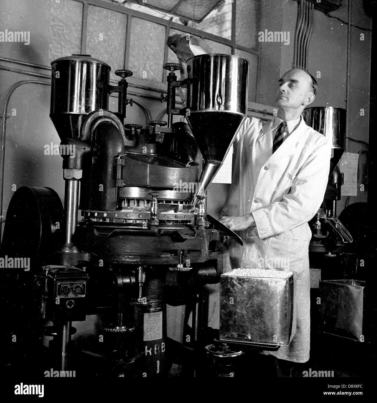 Historical 1950s. England. White coated male puts raw medical material ...