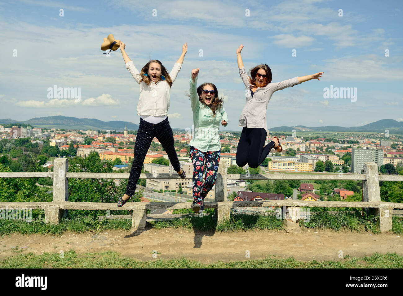 Three young women jumping, with a city panorama behind them Stock Photo ...