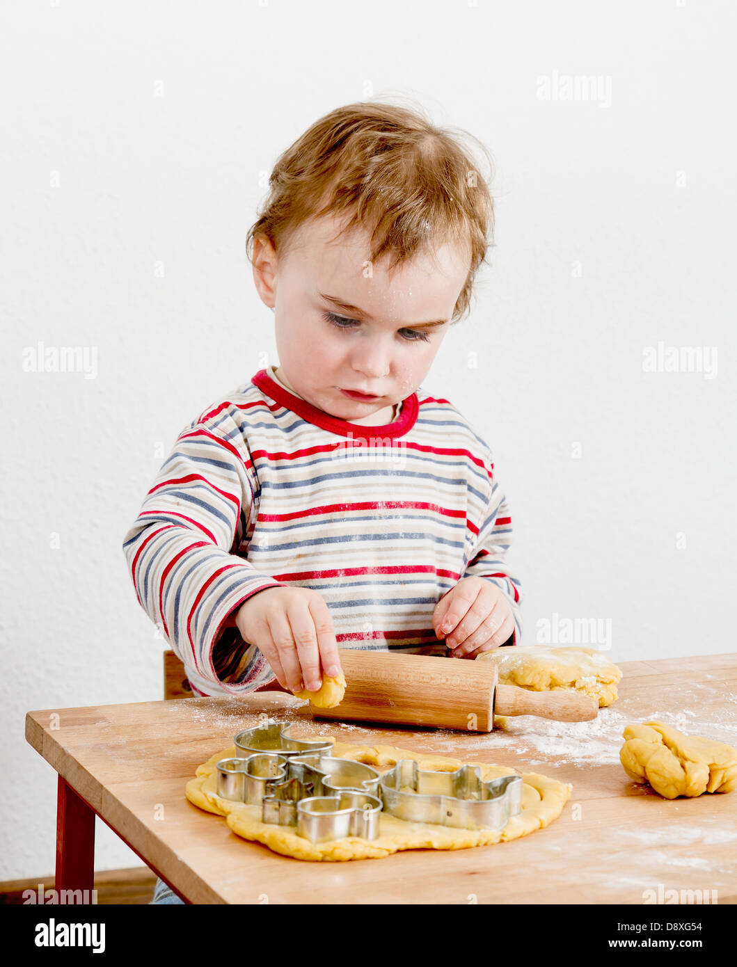 vertical image of 2 year old child making biscuit at wooden desk Stock ...