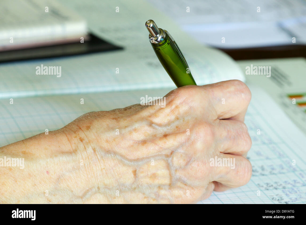 Weathered hand of senior citizen woman with ballpoint pen in hand doing ...
