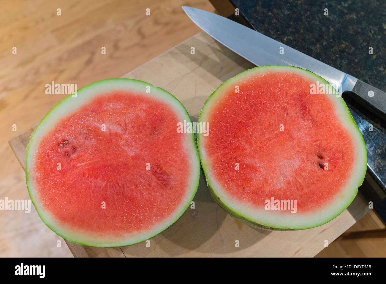 A sugar baby watermelon cut into two halves on a cutting board with a ...