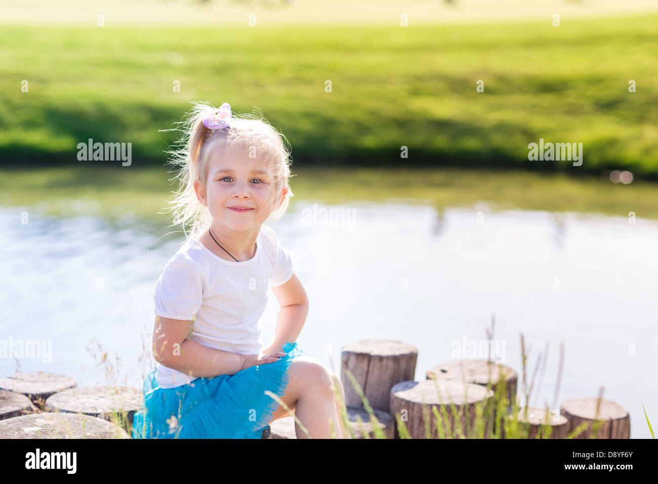 Cute little girl sitting near the lake in summertime in nature Stock ...