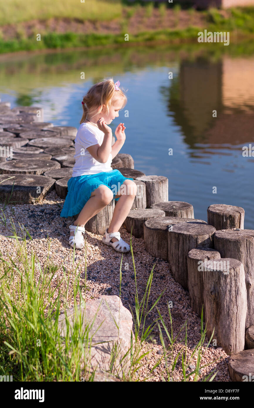 Cute little girl sitting near the lake in summertime in nature Stock ...