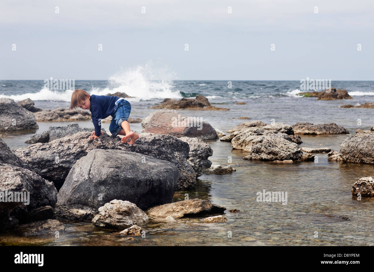 Boy climbing on rocks at beach Stock Photo - Alamy
