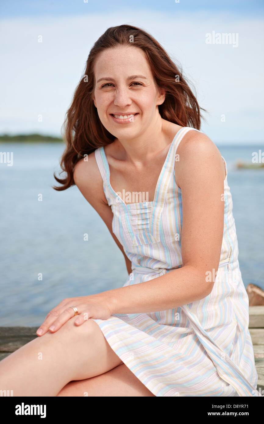 Woman sitting on jetty, smiling, portrait Stock Photo - Alamy