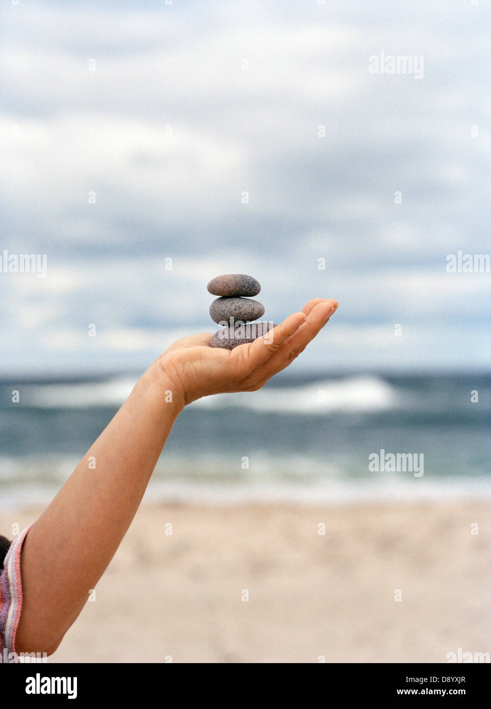 A hand holding up stones with the ocean in the background Stock Photo ...