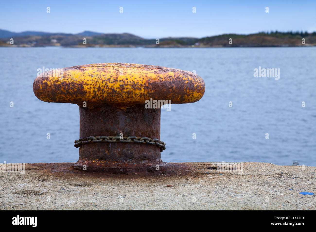 Old rusted yellow mooring bollard with chain on concrete pier Stock ...