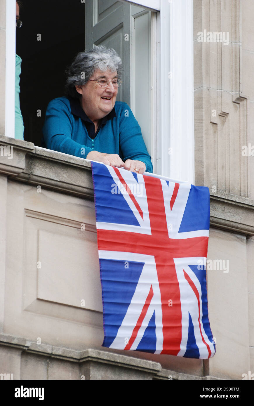 A woman hangs a union jack flag out of a window at a military ...