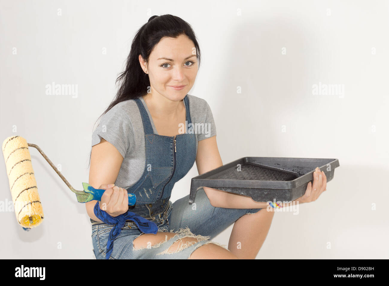 Pretty young woman with a paint tray and roller in her hands crouching ...
