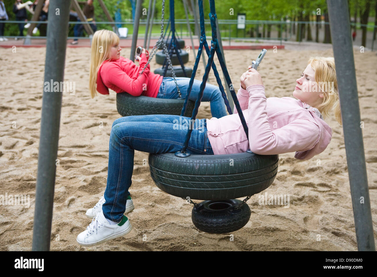 Girls using mobile phones on swings in park Stock Photo - Alamy