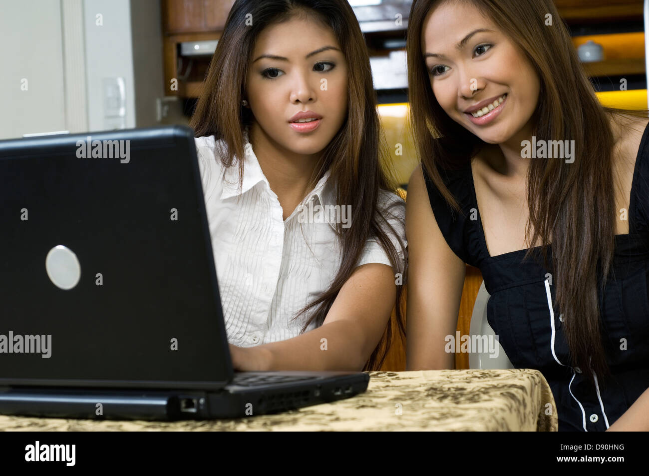 Philippines, two young women working on laptop in kitchen Stock Photo ...