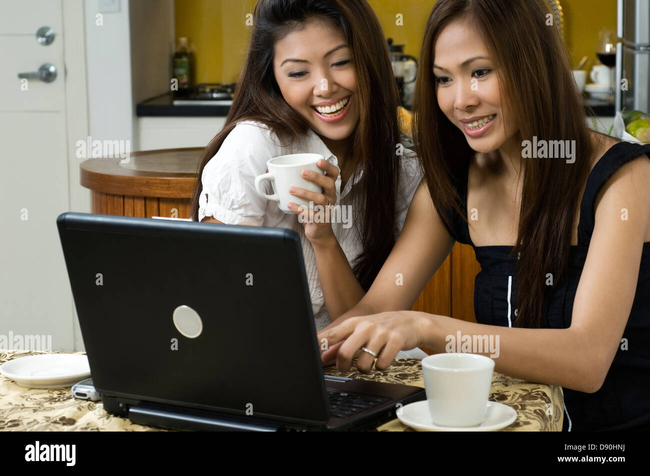Philippines, two young women working on laptop in kitchen Stock Photo ...