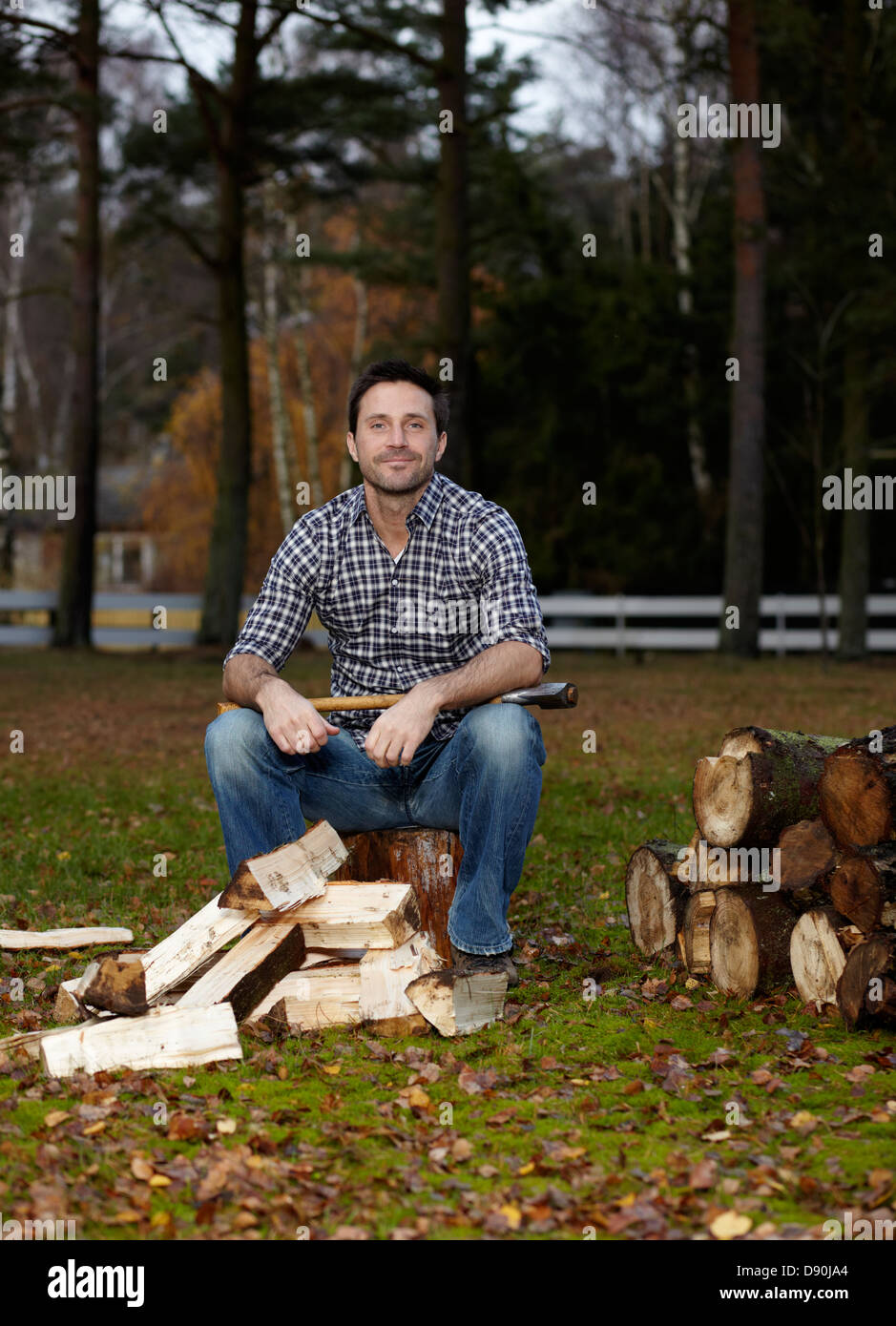 Man sitting on log with axe in his hand Stock Photo - Alamy