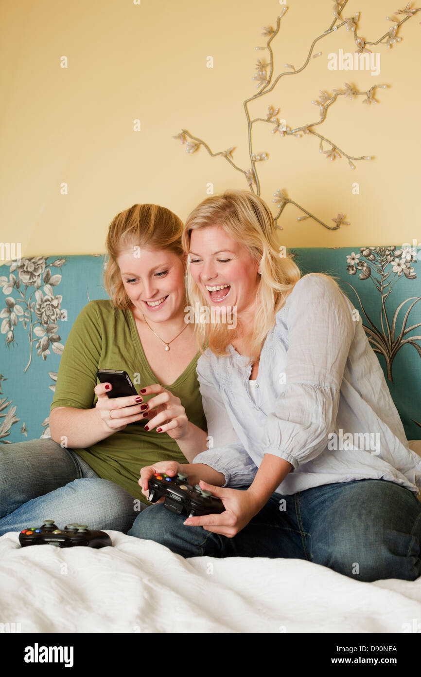 Two young women using mobile phone in bedroom Stock Photo - Alamy
