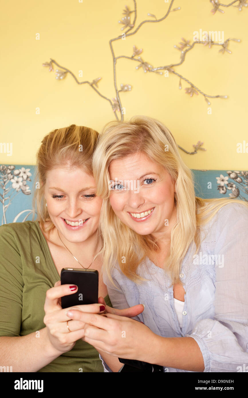 Two young women using mobile phone in bedroom Stock Photo - Alamy