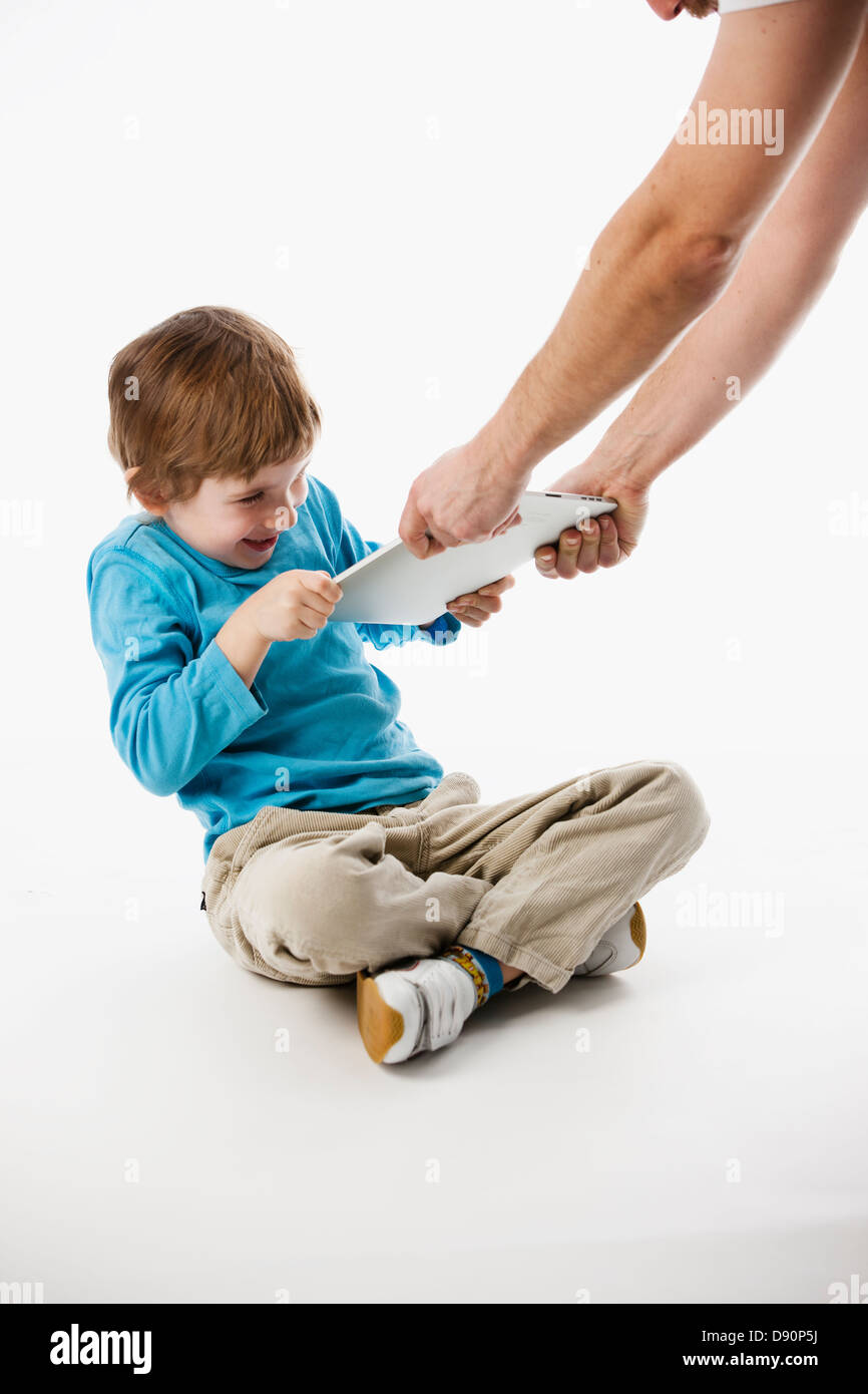 Boy pulling digital tablet from man Stock Photo - Alamy