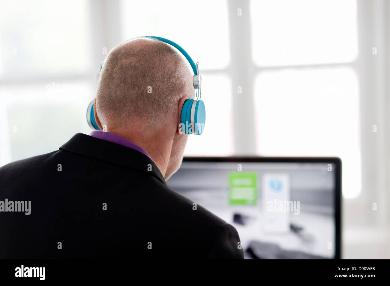 Businessman listening to headphones, using computer in office Stock ...