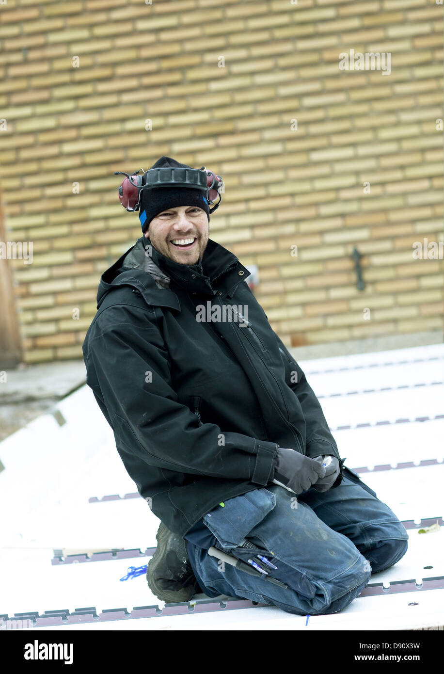 Young construction worker kneeling on roof Stock Photo - Alamy