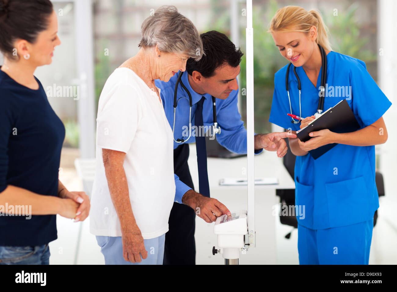 medical doctor monitoring senior patient's weight with his assistant ...