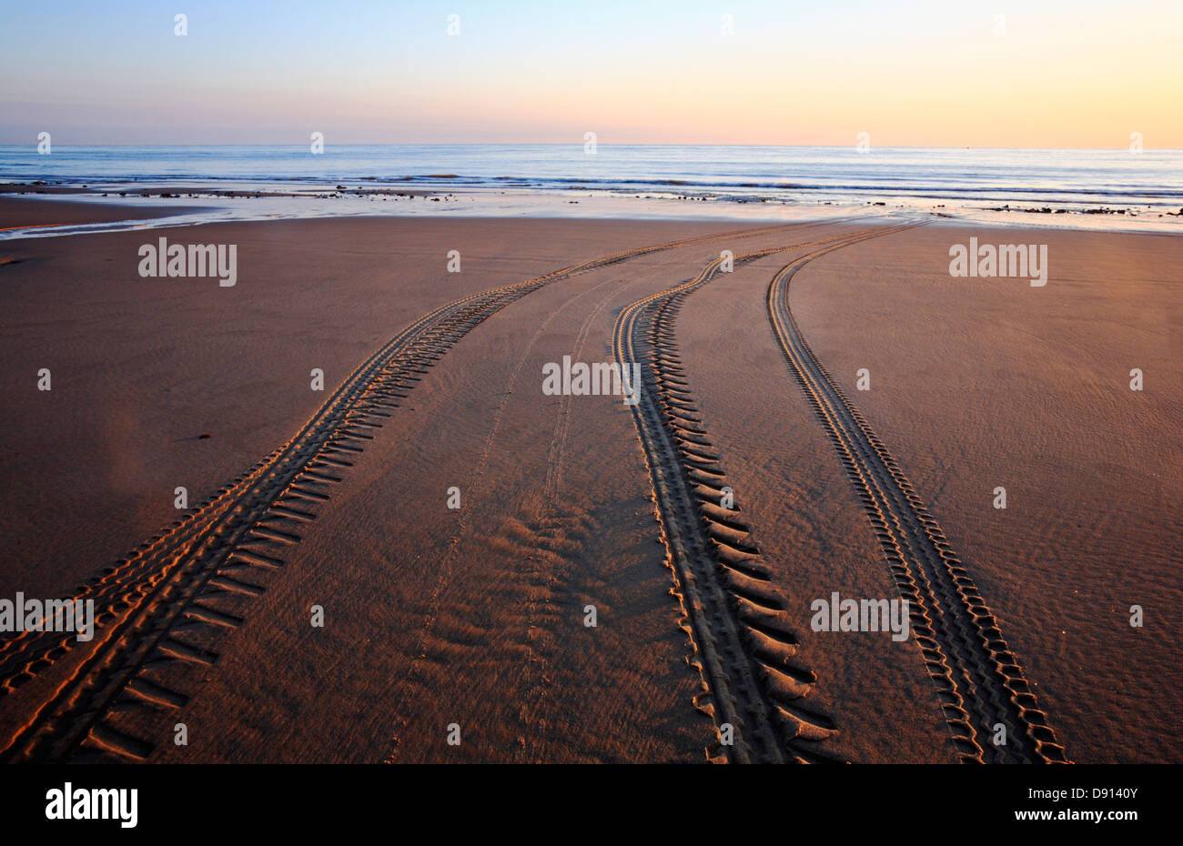 A view of tracks across a beach leading to the sea in early morning ...