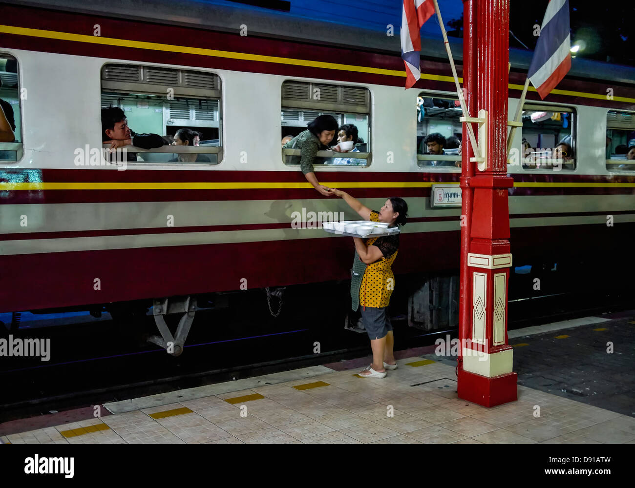 Night scene of a Thai train at the station and passengers buying food ...