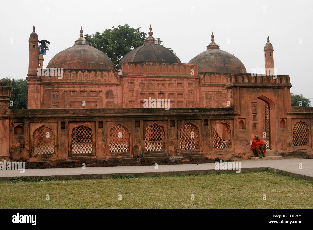 Man sitting by the gate to Shah Niamatullah Mosque, a three-domed ...