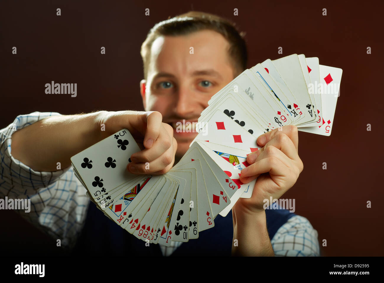 Happy skillful male magician performing playing cards jugglery on dark ...