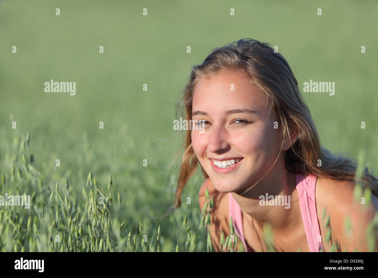 Portrait of a beautiful teenager girl smiling in an unfocused green oat ...