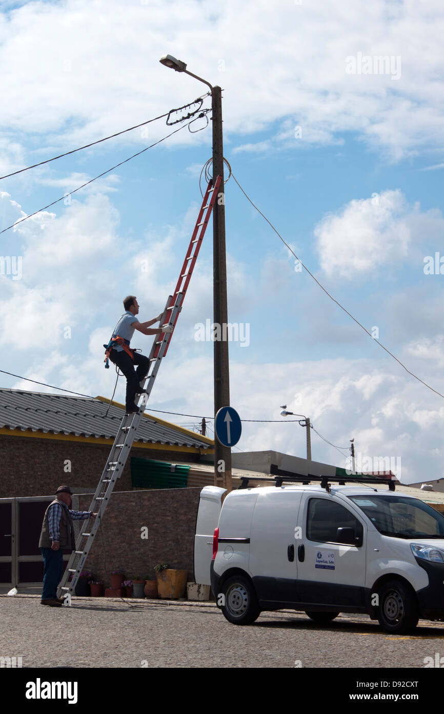 Electricity company man climbing a post while other man holds the stair ...