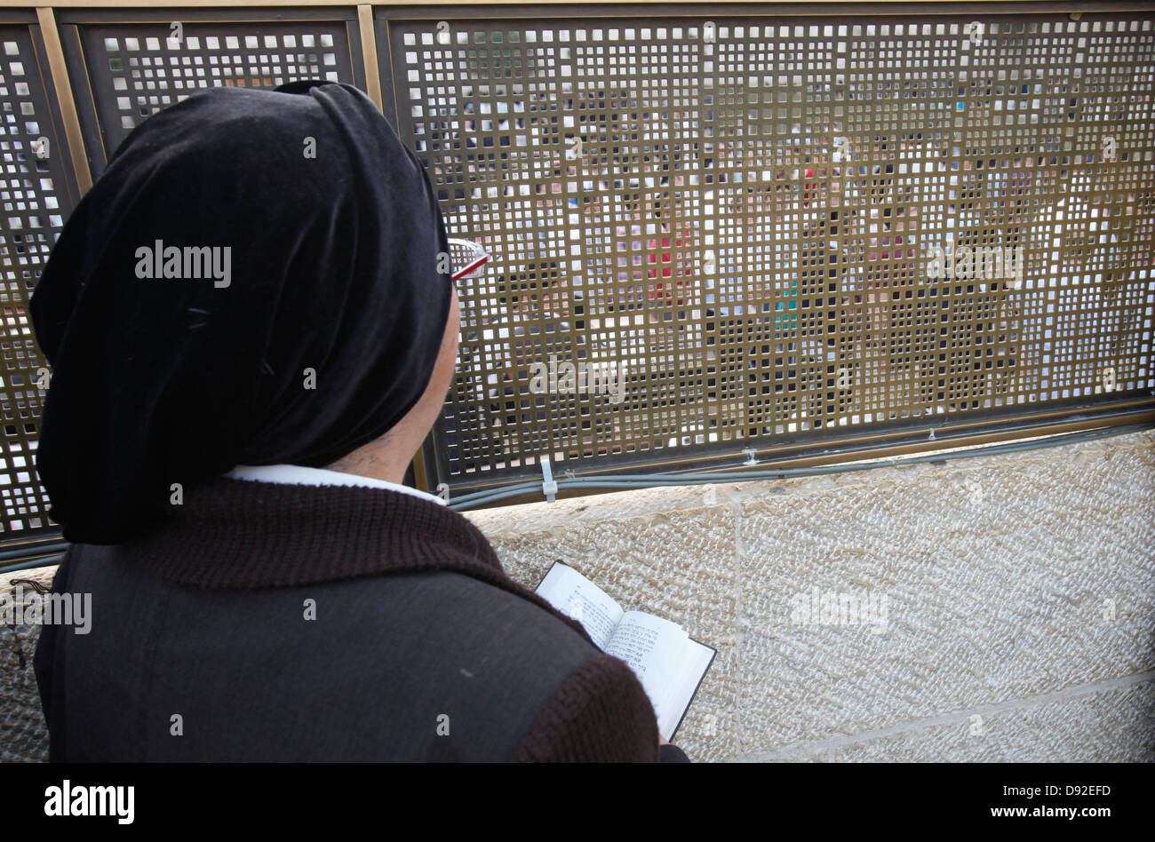 A religious Jewish woman looking through perforated metal fence ...