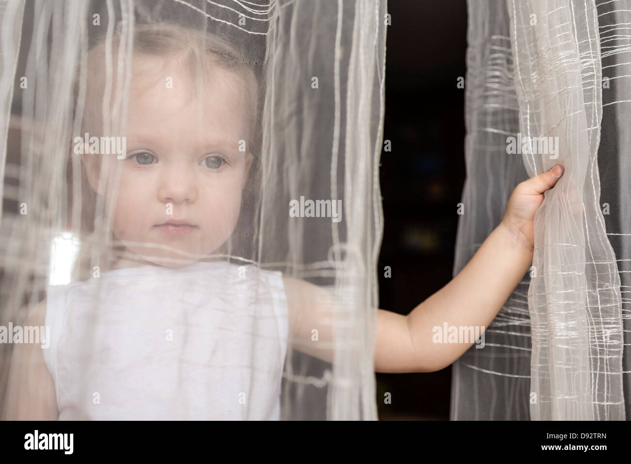 Girl looking out between curtains of open window Stock Photo - Alamy