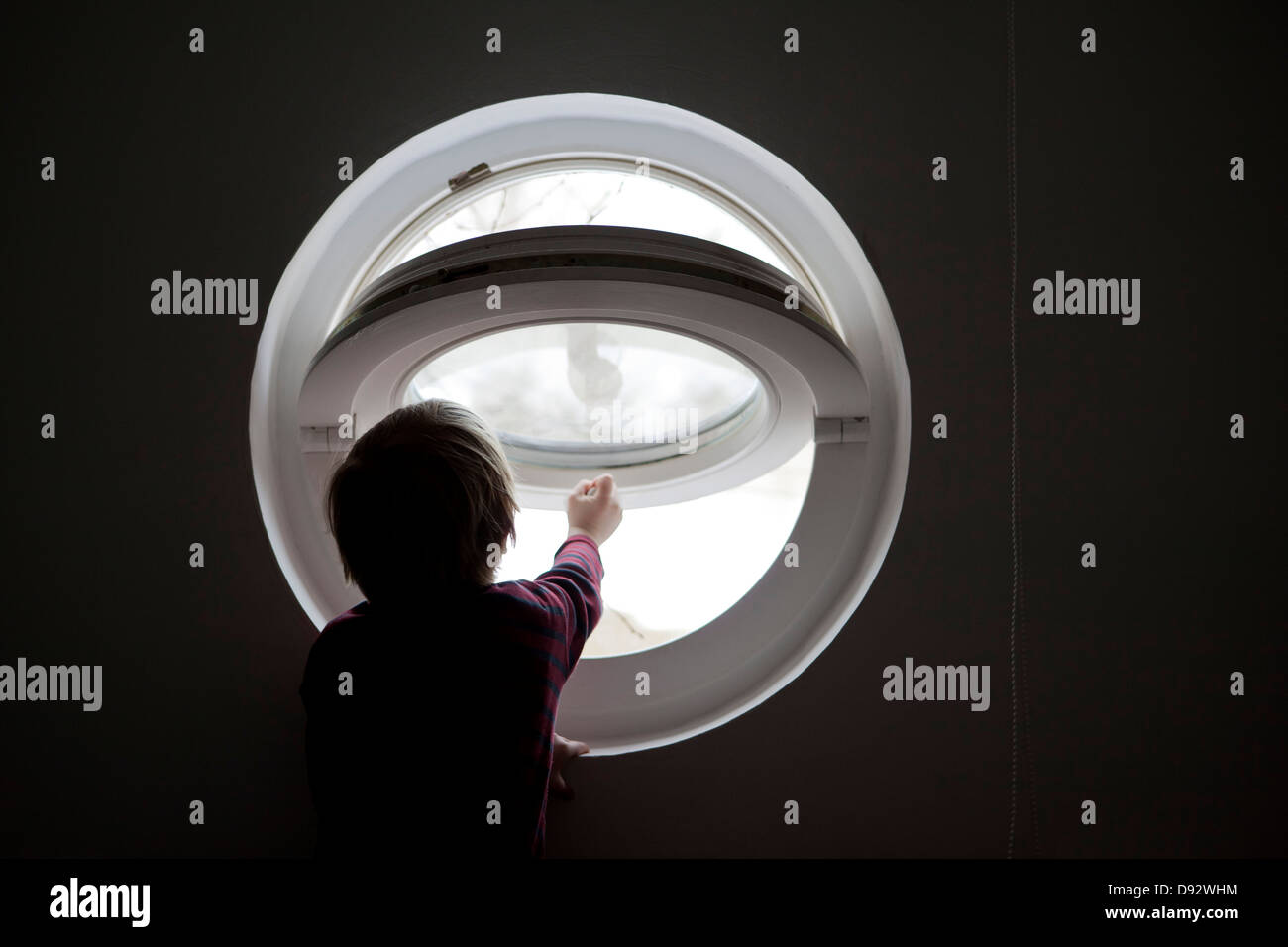 A young boy reaching to open a round window in silhouette Stock Photo ...